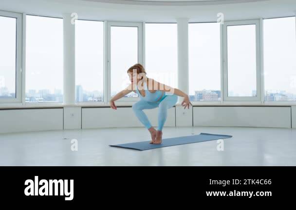 Young blonde woman practicing variation of Crow Pose in yoga studio ...