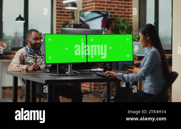 Asian digital editor looking at greenscreen on multiple monitors ...