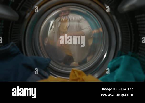 Man with laundry basket opens the door of the washer and takes out the ...