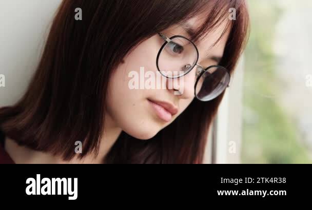 In a poignant scene, a teenage girl sits by the window, her face marked with sadness and ...