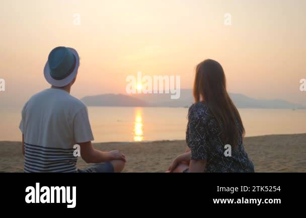 Caucasian man and his wife sitting at the beach and then kissing. Back ...
