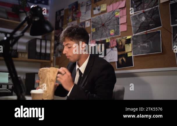 Detective eating hamburger in his office, private detective looking at ...