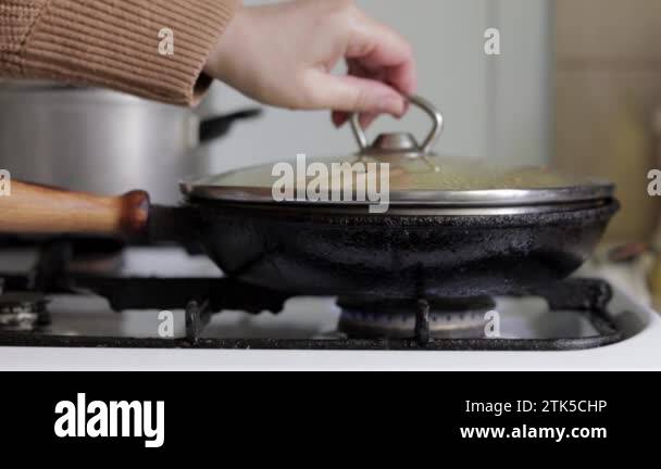 A womans hand opens the lid of a frying pan with fried potatoes, a lot ...
