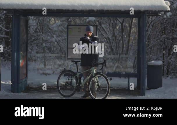 Frozen male cyclist waiting for bus at halt stop with bicycle in winter ...