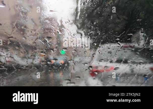 Rain falling on car windshield view. Drive car on traffic jam street at ...