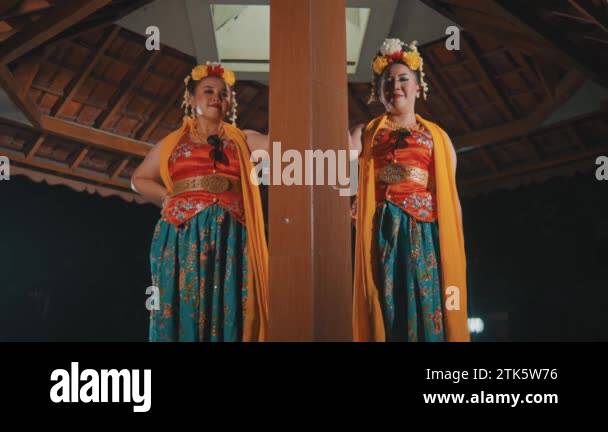 Two traditional Javanese dancers are standing between the pillars of a ...