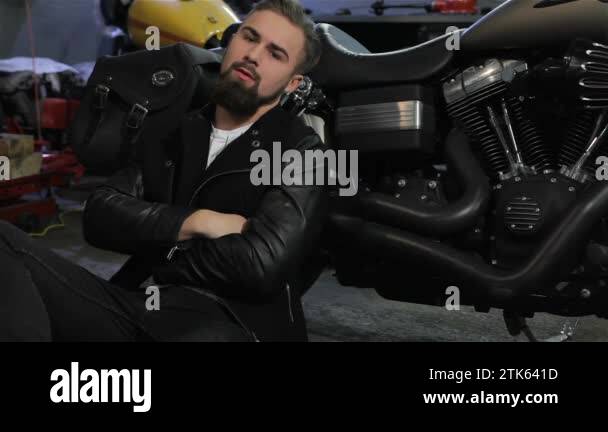 Male biker sitting on the floor near the motorcycle. Young man in black ...