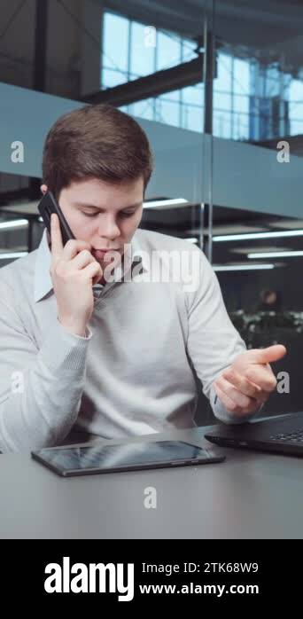 Vertical Screen: Young man wearing sweater working in office, using ...