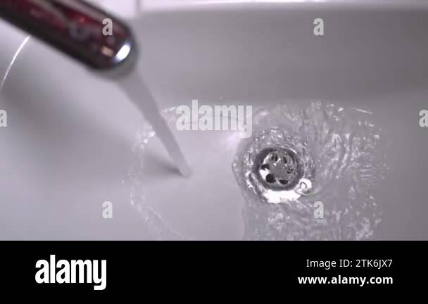 Close-up stainless steel sink hole filled with water. Water pours from ...