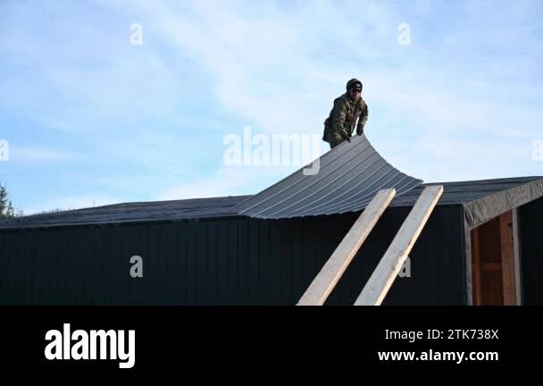 Male builder installing black corrugated iron sheet used as facade of ...