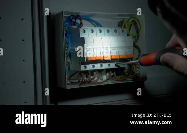 Electrician assembles electrical panel in dark by light of flashlight ...
