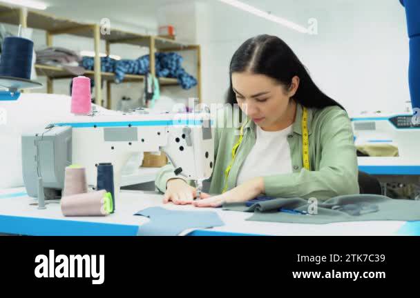 Portrait of a professional seamstress in a textile factory sewing with ...