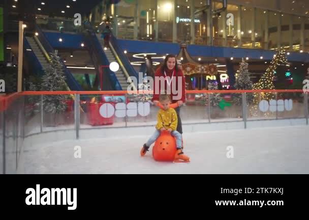 Mom with daughter have fun on ice skater rink use skating aid dolphin ...