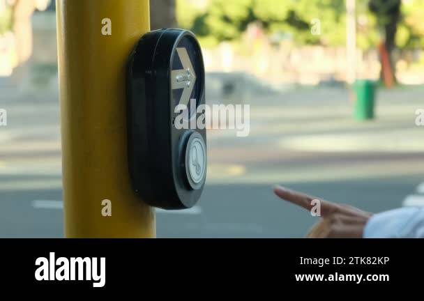 Female pedestrian presses a traffic light button to cross the road. The ...