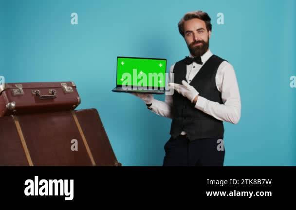 Classy bellhop presents greenscreen on laptop display in studio while ...