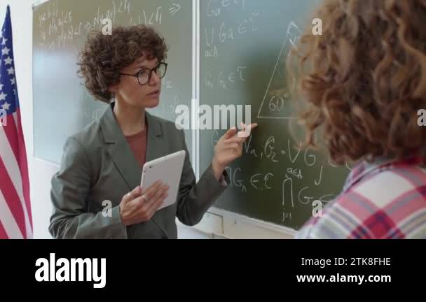 Female Math teacher standing in front of her student explaining how to ...