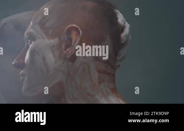 Well-built athletic male bodybuilder in white clay runs his hand ...