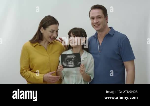 Young parents and their daughters look at ultrasound film approaching ...