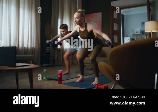 Active millennial family training with dumbbells at home. Smiling young couple making sport ...