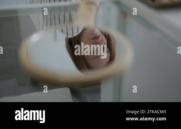 A woman s face is reflected in a mirror on a glass table as she ...