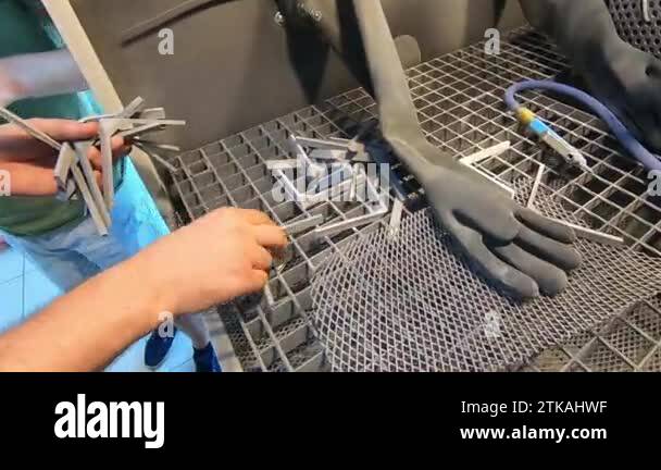 A male worker picks up 3D printed metal models after cleaning them in a ...