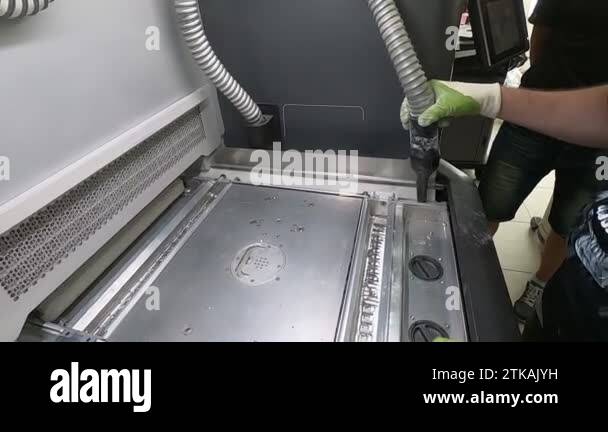 A male worker cleans the surface of an industrial 3D printer from white ...