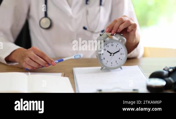 A doctor with an alarm clock and a toothbrush in his hands, a closeup. Hygienic procedure for ...