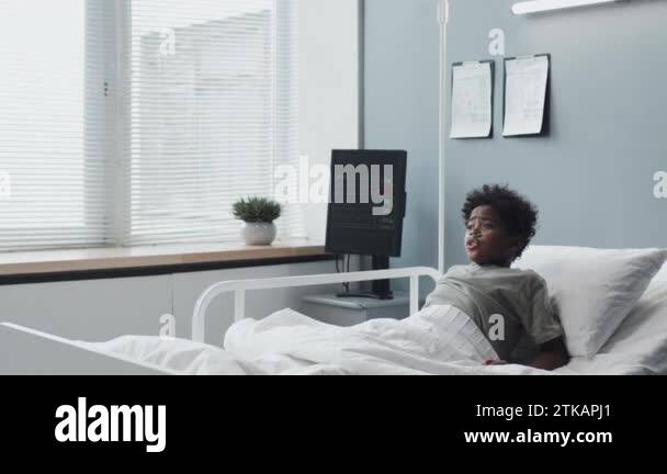 Medium long of Black boy with oxygen tube in nose sleeping in hospital ...