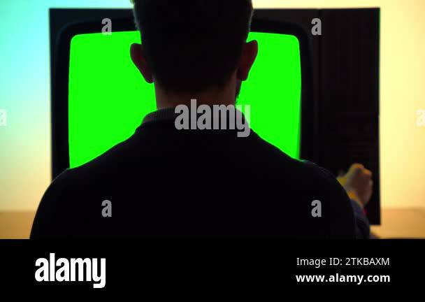 Back view shot of male person sitting in front of vintage TV with ...