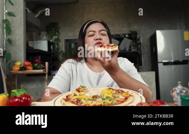 Obese Asian woman sits and eats her favorite glutton snack food pizza ...