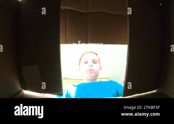 Small red-haired boy with freckles opening carton package and pulling ...