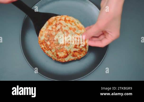 Female hands put a delicious first pancake with cheese on a black plate ...