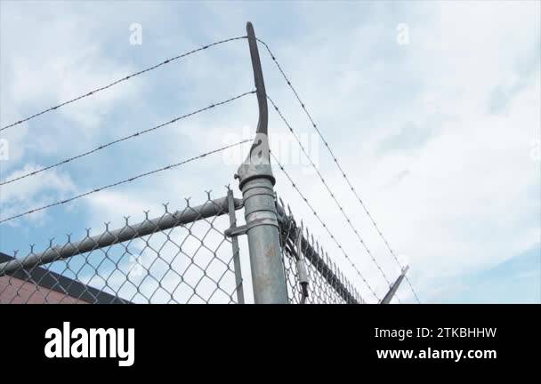 three lines of barbed wire at top of silver fence corner with sky ...
