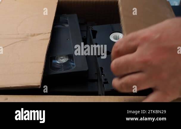 Old VHS tapes in a cardboard box. A man opens a cardboard box with VHS ...