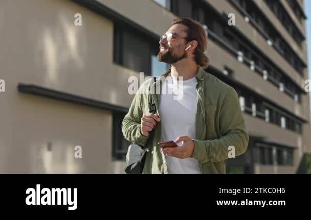Side view of brunette man with earphones and sunglasses carrying ...