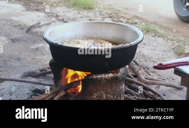 close up of bananas are being fried in boiling oil. Vendor keeping the fire burning in wood ...