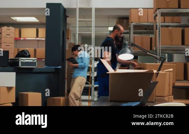 Young office employee arranging goods in packages, using laptop to plan ...