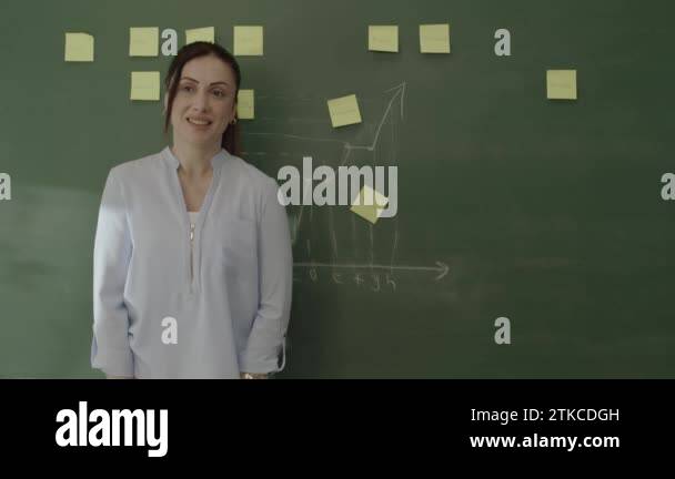 Female teacher standing in front of blackboard with glued notes and ...