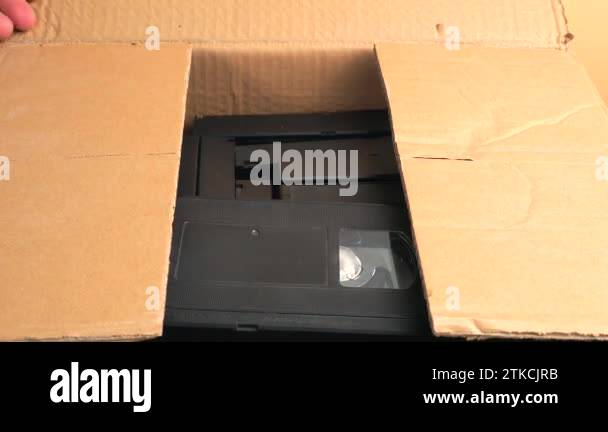 Old VHS tapes in a cardboard box. A man opens a cardboard box with VHS ...