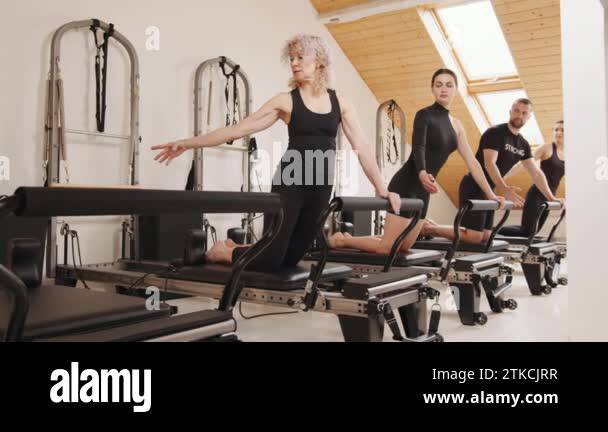 Skilled senior female trainer woman in front split on pilates reformer ...