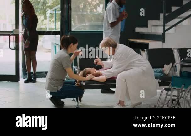 Little girl fainting in waiting area lobby and medic using flashlight ...