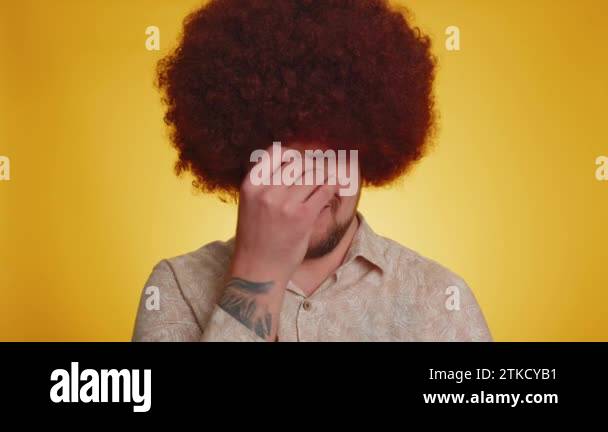 Upset disappointed bearded hipster man with lush afro hairstyle wipes ...