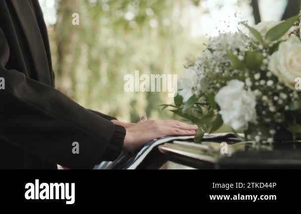 Grieving widow in black coat and eyeglasses putting her head on casket ...