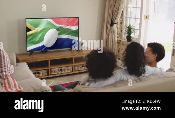 Biracial family watching tv with rugby ball on flag of south africa on ...