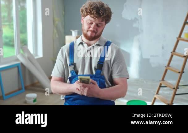 Repairman worker in blue overalls is counting money, smiling and ...