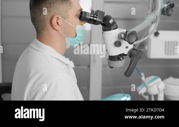 A dentist performs a surgical procedure under a microscope to treat a ...