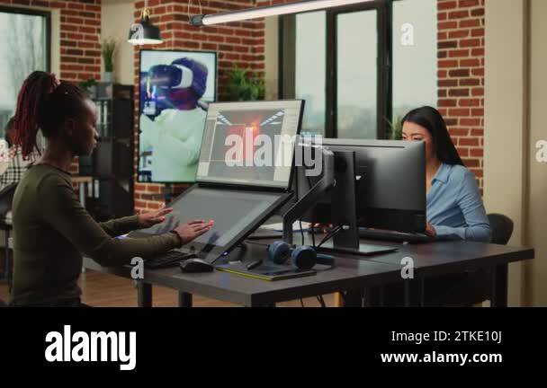 Female creative engineer using game programming software on computer and touchscreen, working ...