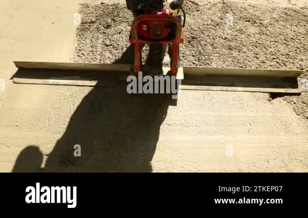 Construction worker is leveling fresh concrete with motor power tool ...