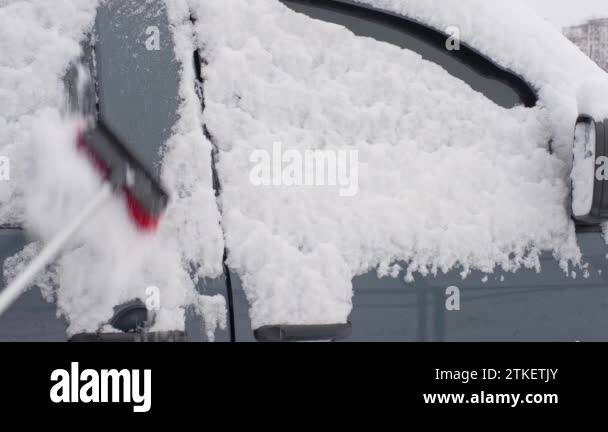 Man brushing fresh snow from his car with a brush. The streets are ...