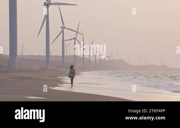 Rows of wind turbines spin on the beach as a woman in a bikini strolls ...
